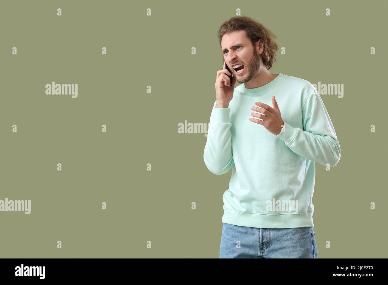 Angry young man talking by mobile phone on green background Stock Photo ...