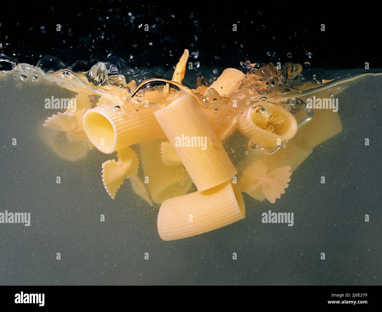 pasta rings falling in the boiling water on dark background. Underwater ...