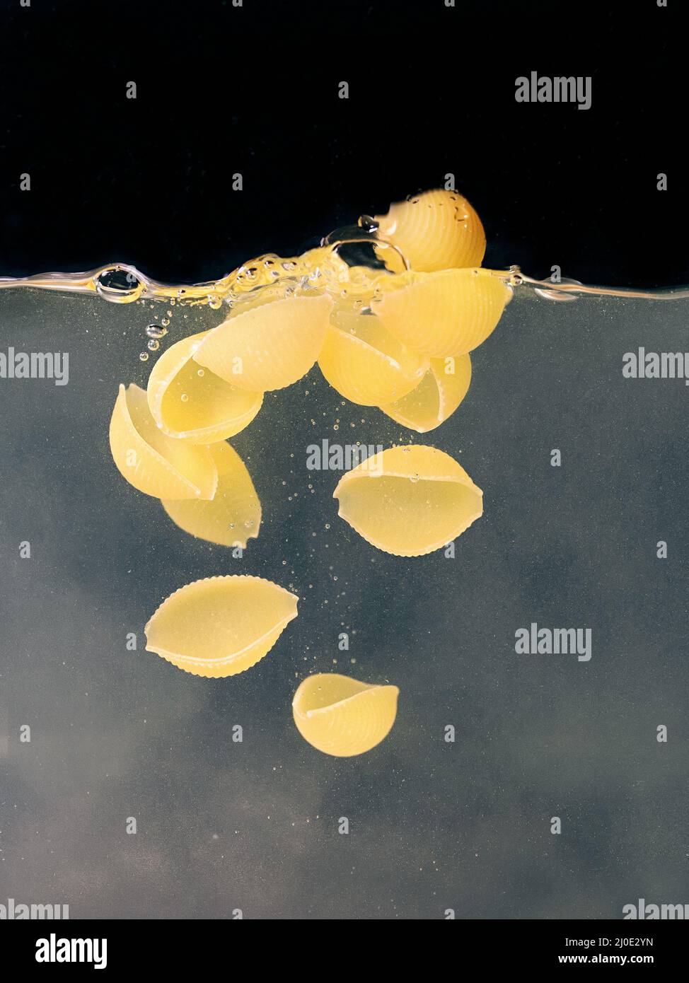 butterflies pasta falling in the boiling water on dark background ...