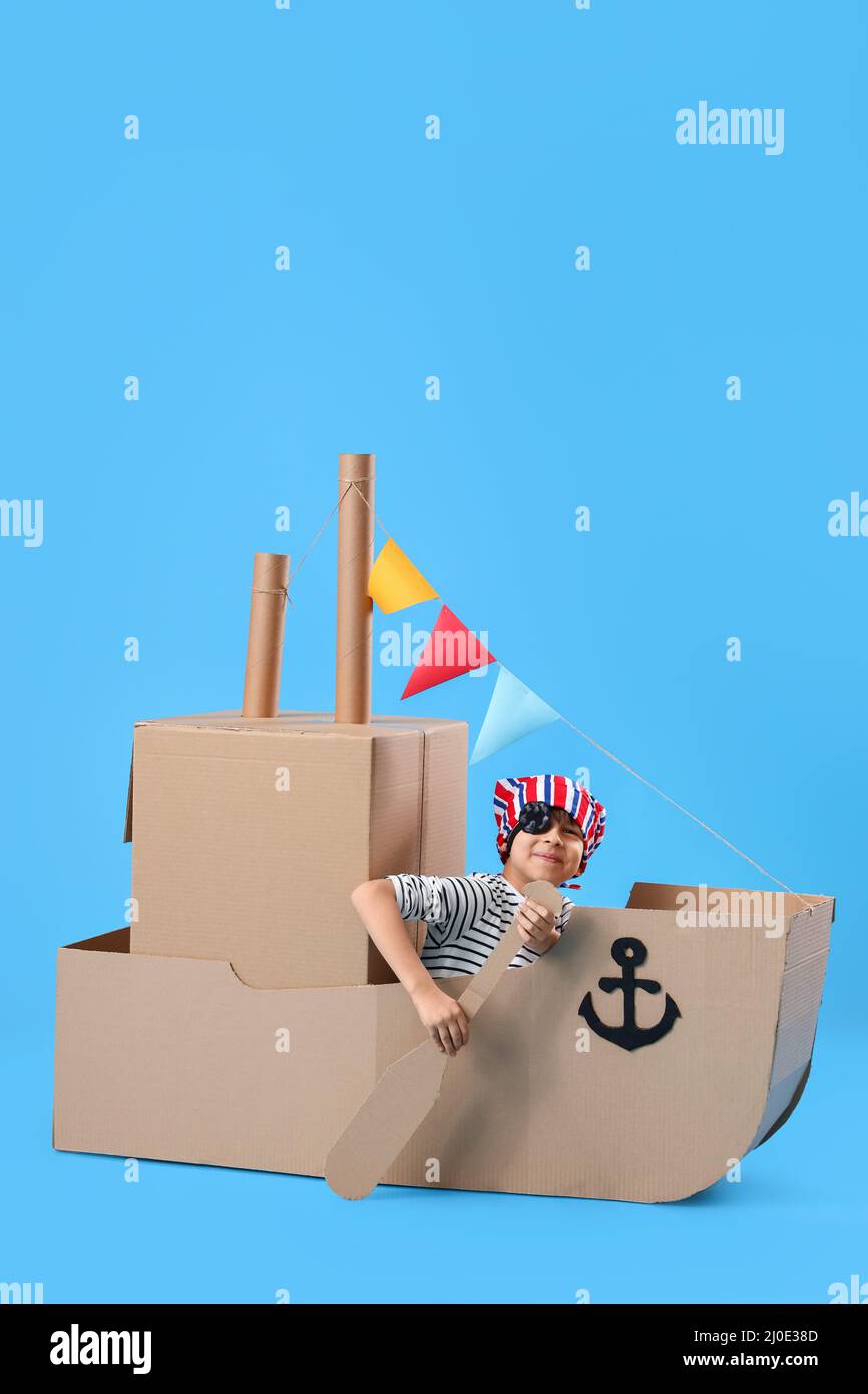 Cute little boy playing with cardboard ship on blue background Stock ...