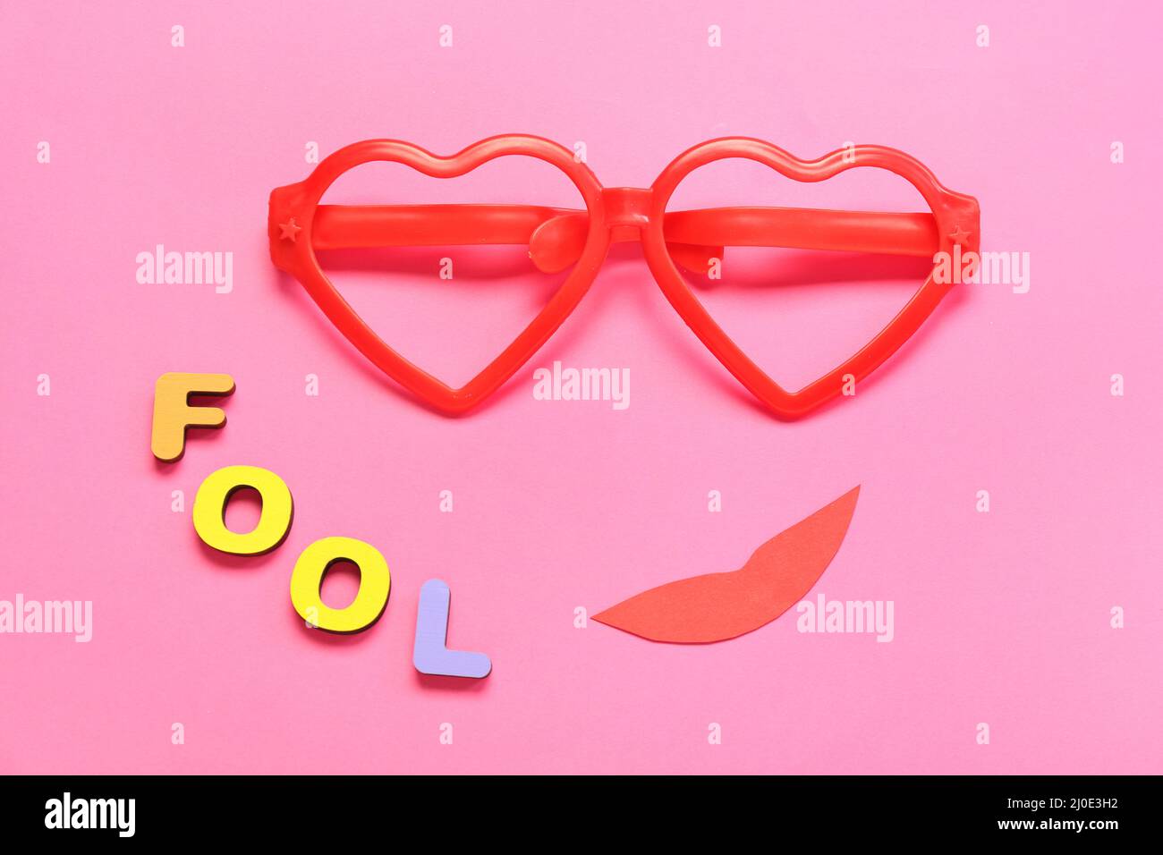 Composition with heart shaped eyeglasses, smile and word FOOL on color ...