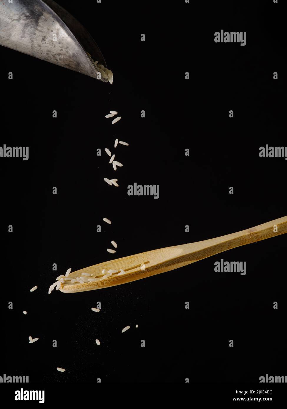 Rice grains on a wooden spoon in frozen flight on a black background ...