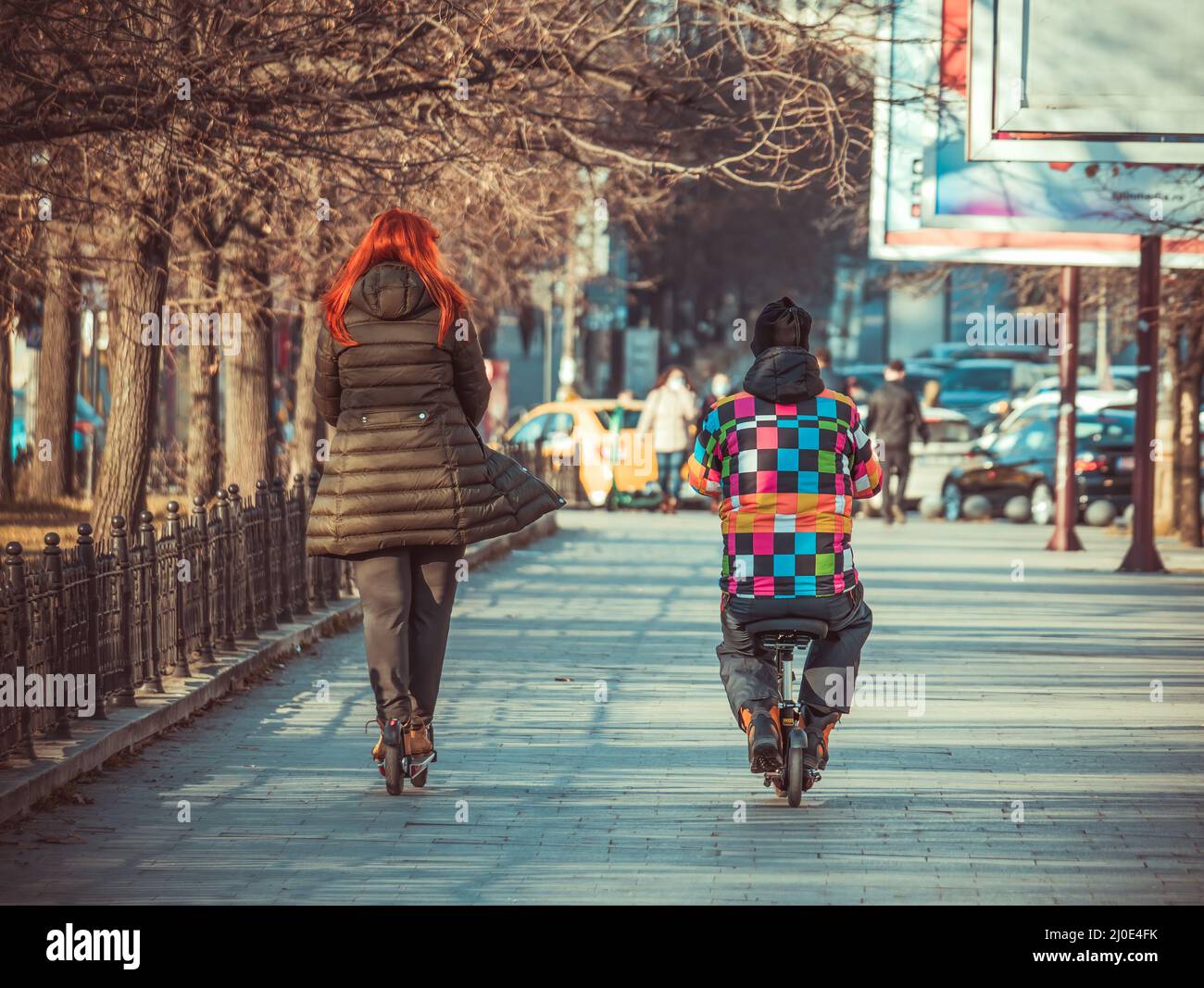 Rear view with two people riding electric scooters on the sidewalk in ...