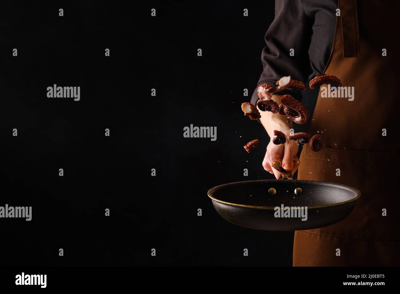 A professional chef in a dark uniform cooks octopus pieces in a pan in ...