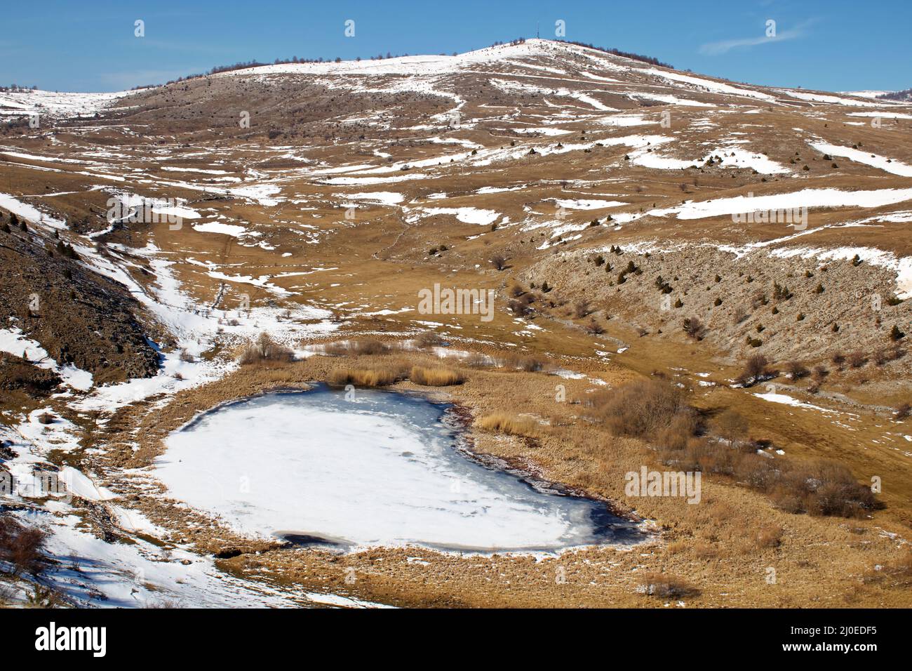 Fully frozen small lake or pond on the valley with golden grass and ...