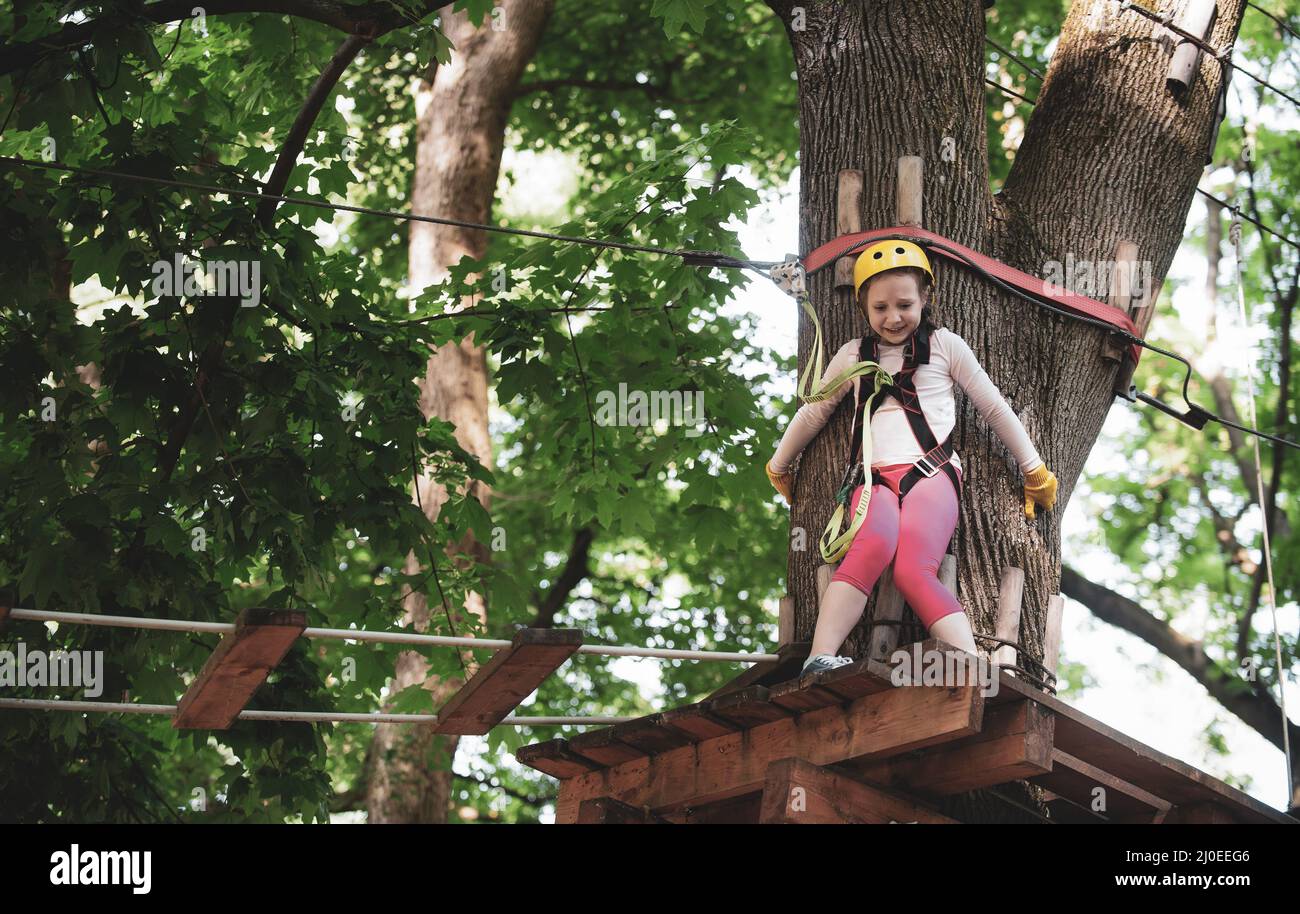 Kid climbing trees in park. Rope way - little girl is looking at the ...