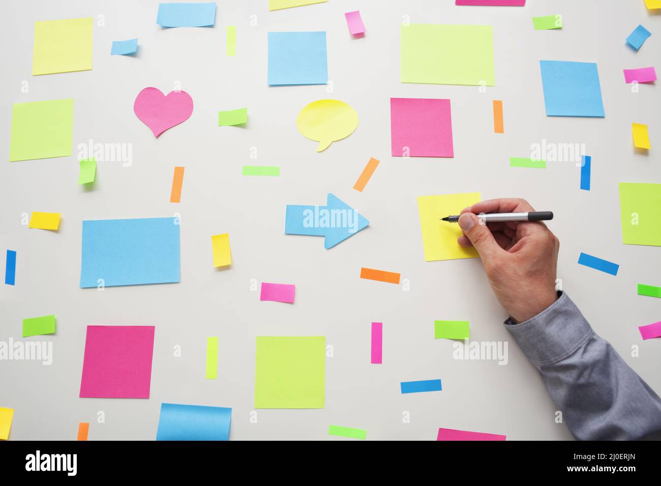 Businessman writing onto a post it note, surrounded by assorted post it ...