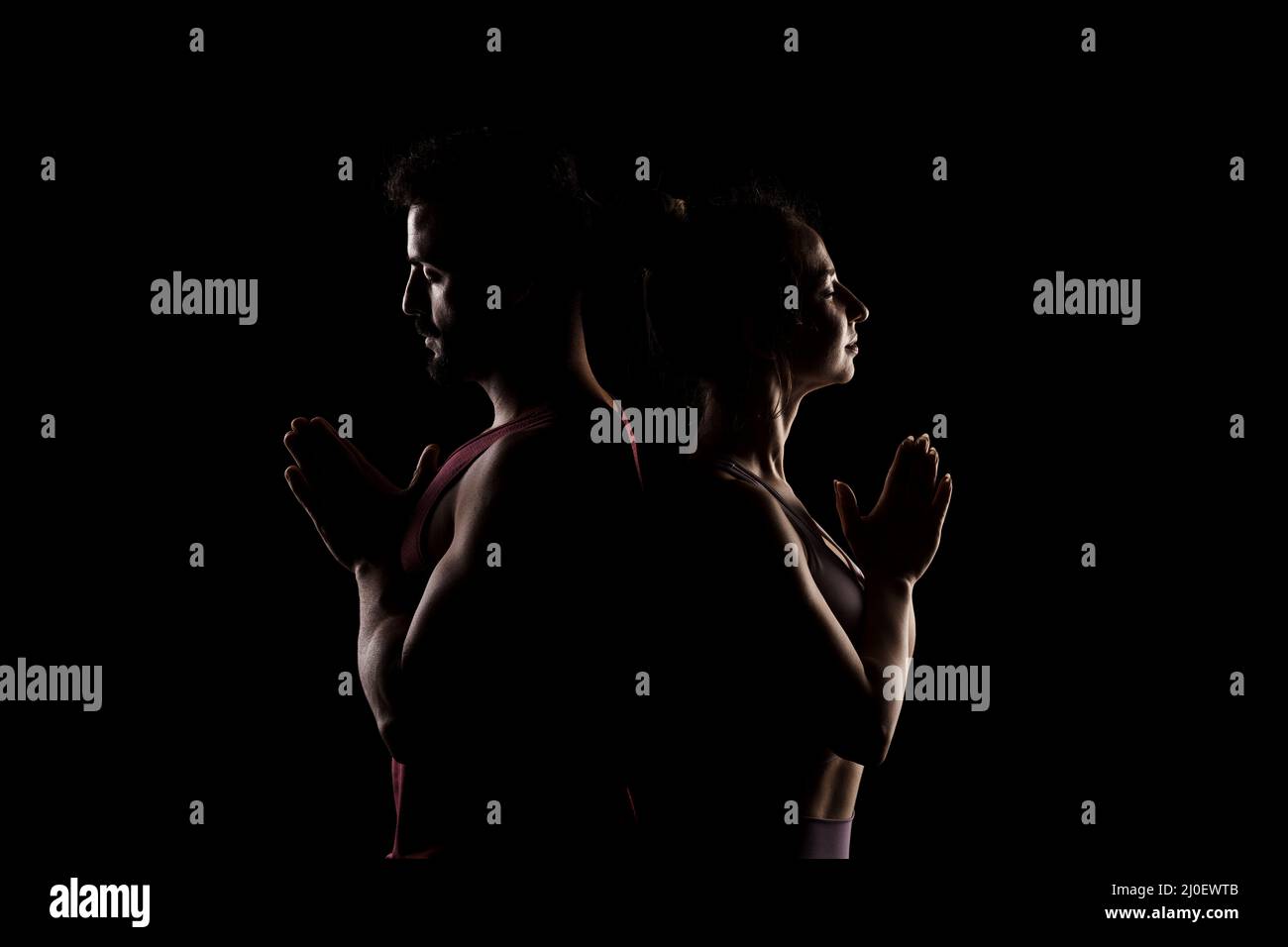 Fit couple posing together. Boy and girl praying back to back side lit ...