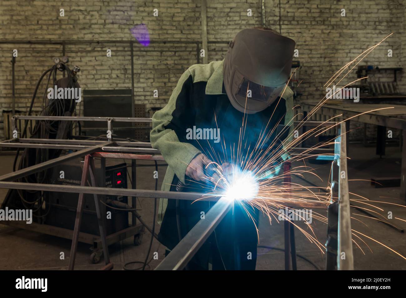 Welder welding a metal part in an industrial environment, wearing ...