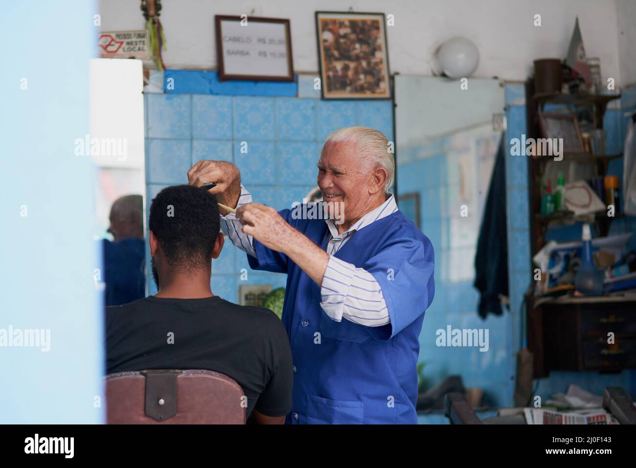 He loves his line of work. Shot of a senior man trimming a clients hair ...