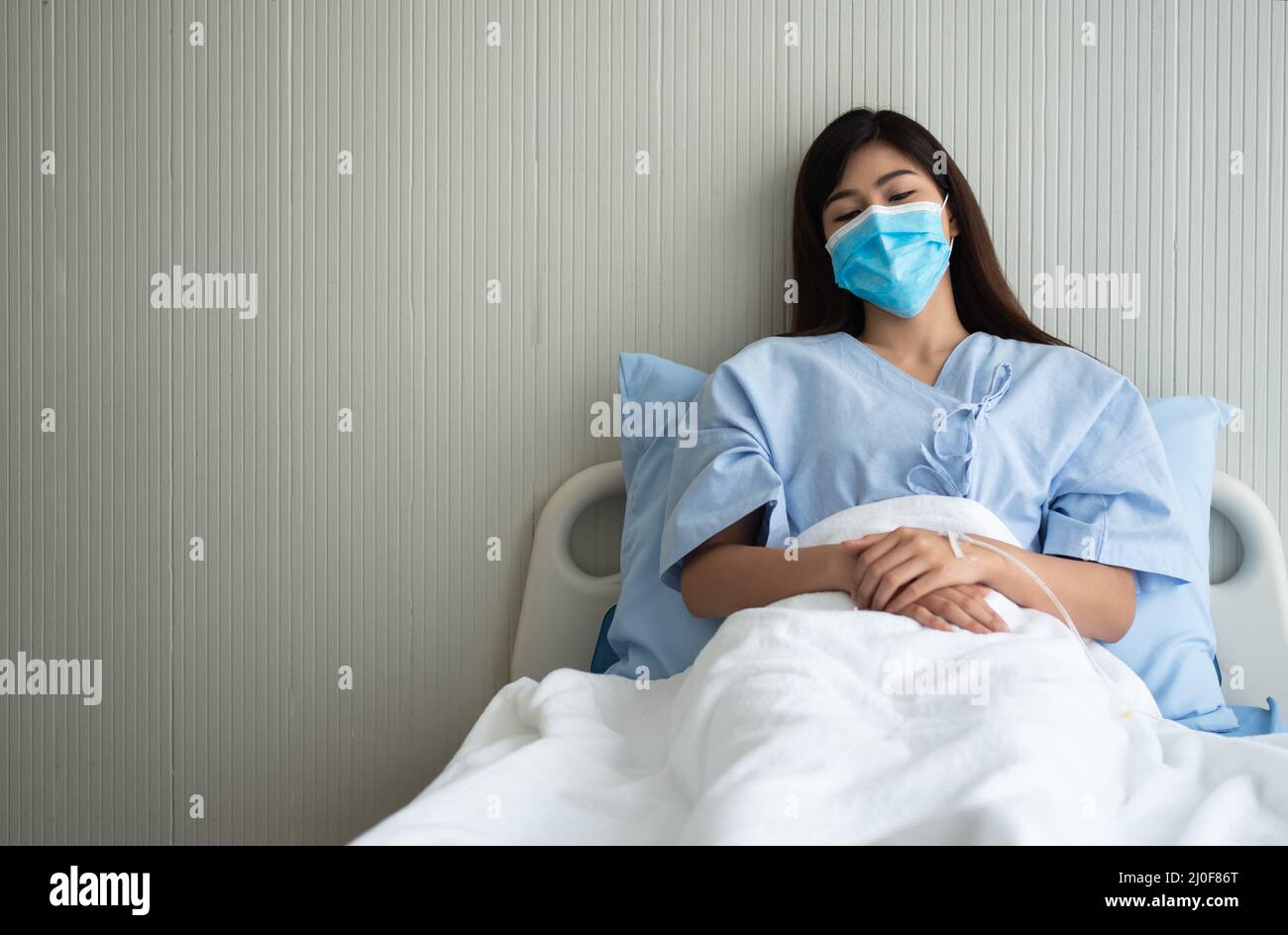 Sad Asian patient woman lying on the hospital bed and wearing a face mask to protect coronavirus ...