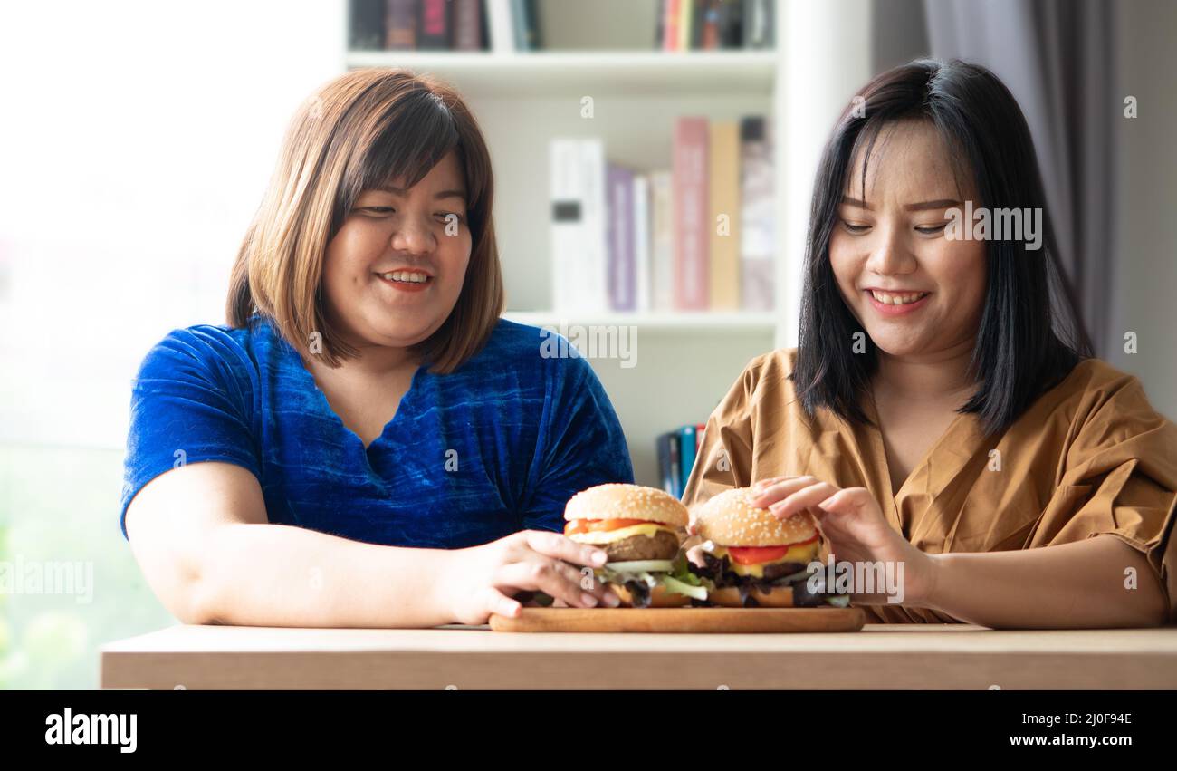 Hungry overweight woman holding hamburger on a wooden plate, During ...