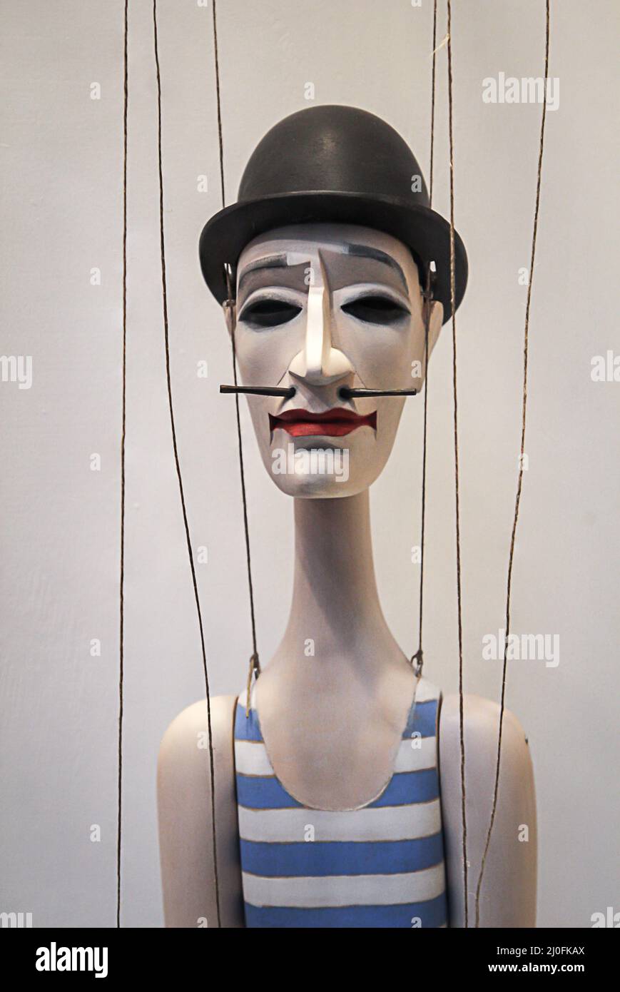 A wooden figure with a pointed beard and a bowler hat hangs on threads ...