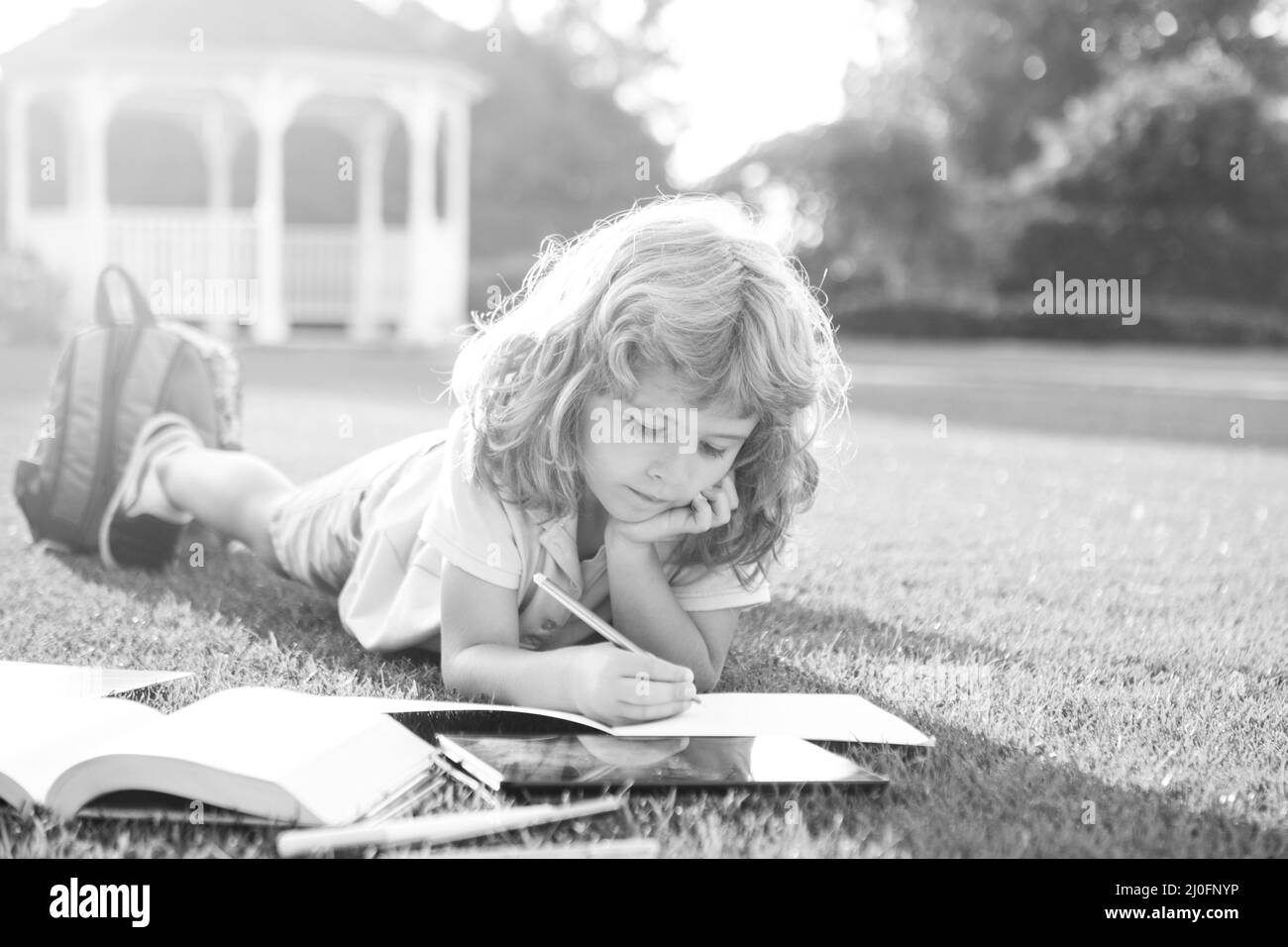 Beautiful child boy with book writing notes in copybook on grass ...