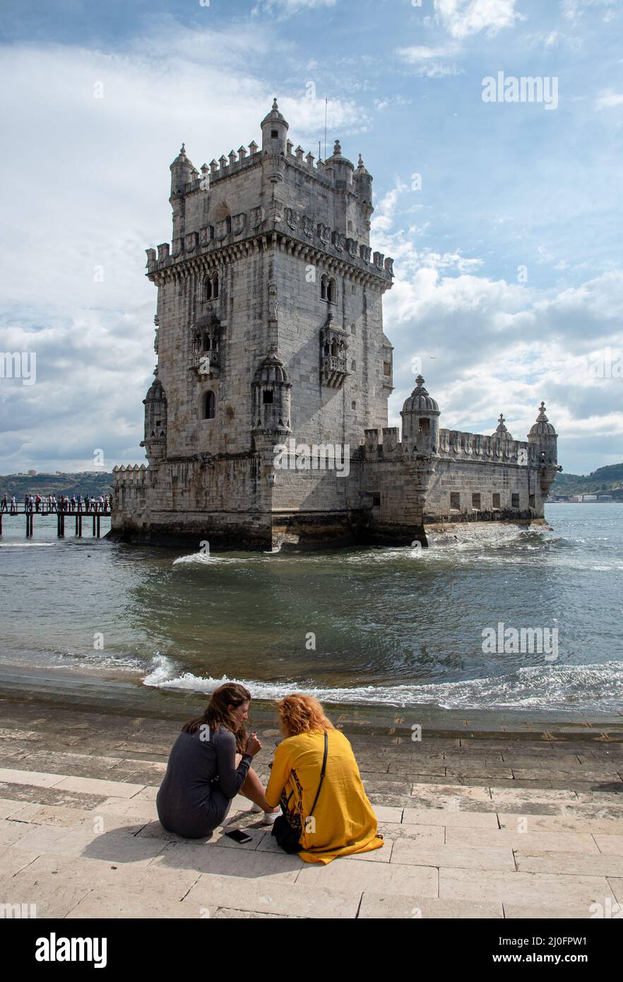 Tourist girls sitting in front of the Belem Tower at Tagus River, in ...