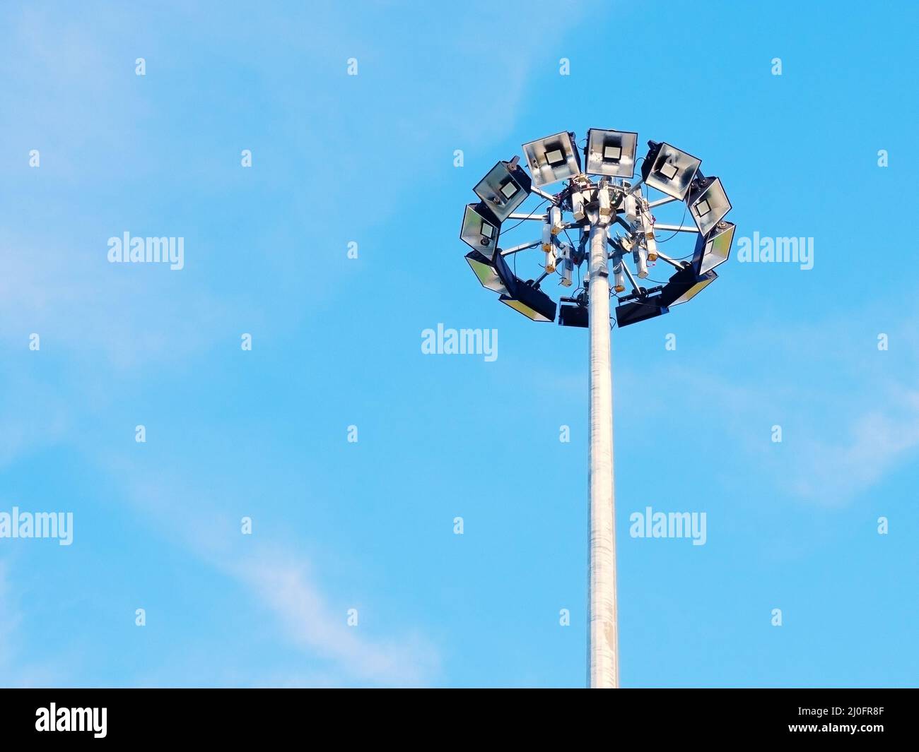 High lamppost with many spotlights in a circle against the blue sky ...