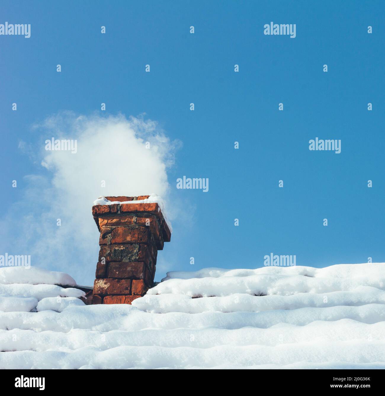 Smoke out of a brick chimney on a snowy rooftop home on the background ...