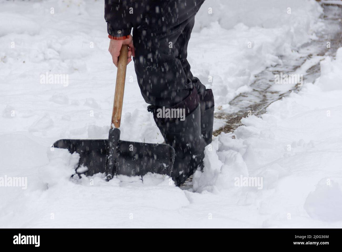 A man cleans winter paths in the yard with a shovel from snow in the ...