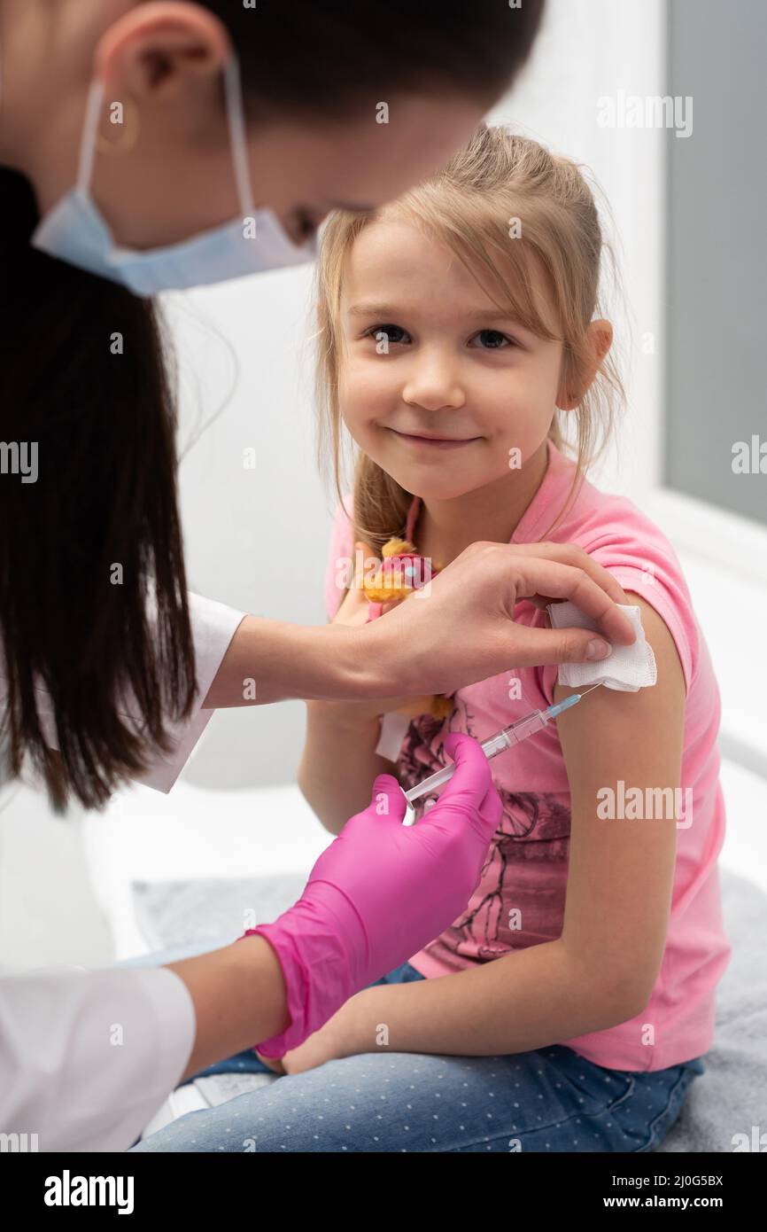 While receiving the vaccine, the smiling girl looks straight into the ...