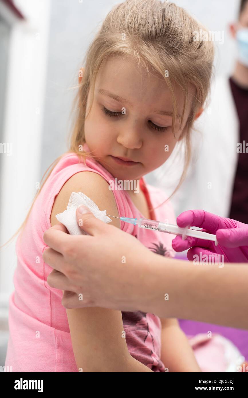 The doctor is giving a little girl an injection. The child stares in a ...