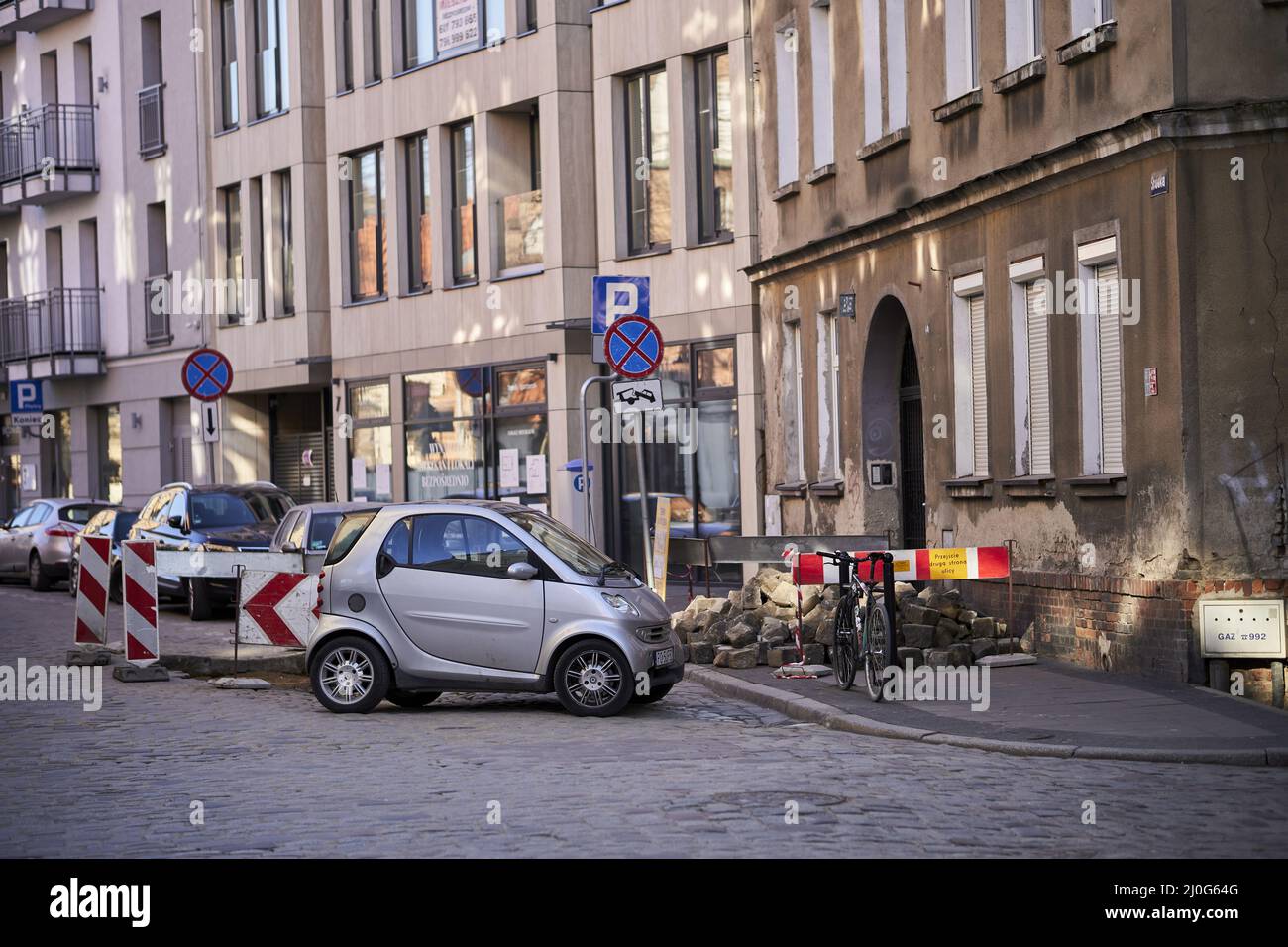 Parked small car and construction work with barrier by old buildings in ...