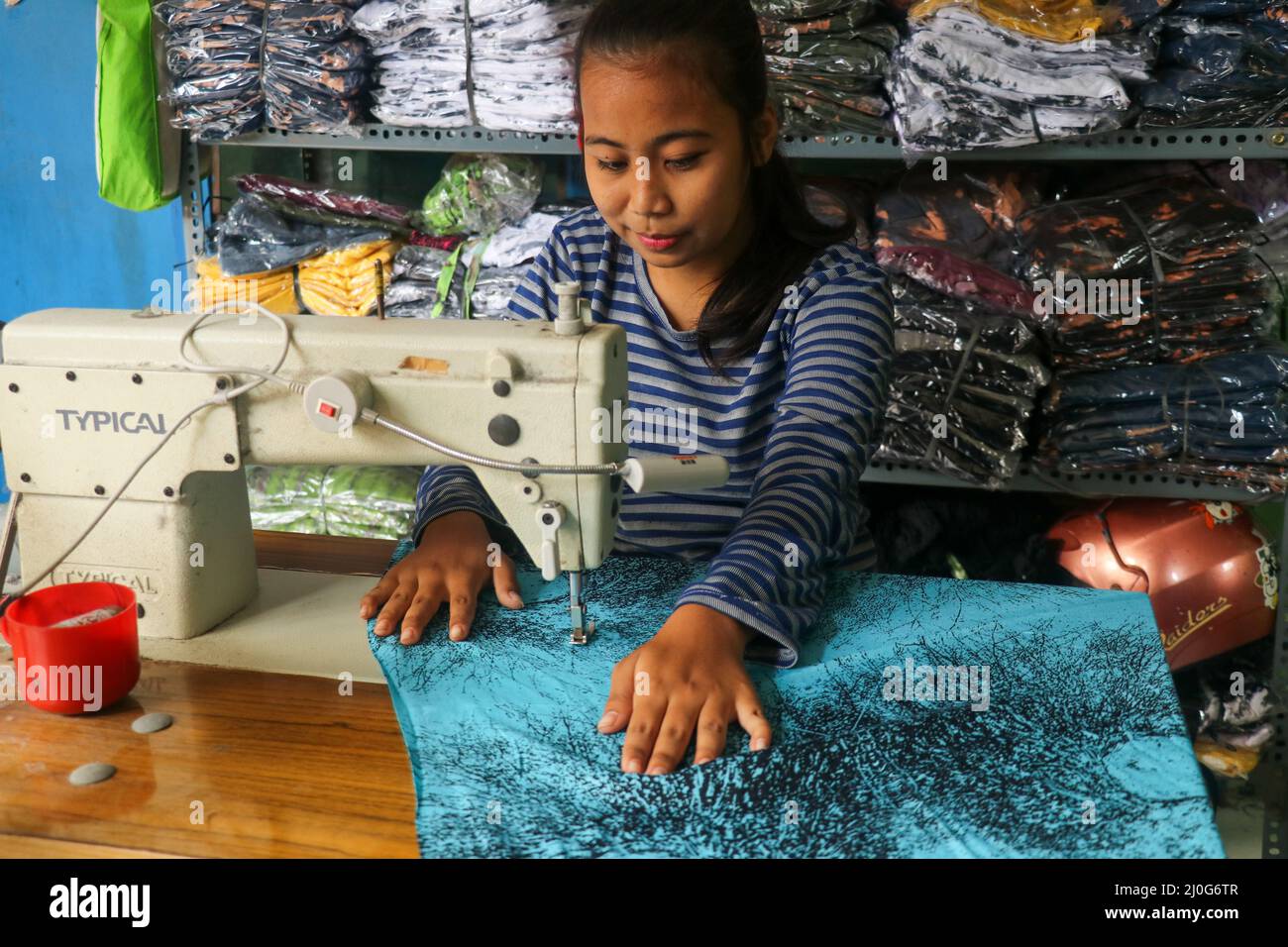Asian dressmaker woman sews clothes on sewing machine. Smiling in ...