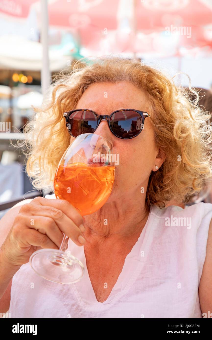 attractive woman drinks a red colored drink like Aperol Spritz ...