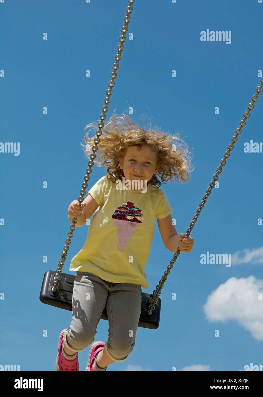 Child swings high. With blue sky in background. Portrait format Stock ...