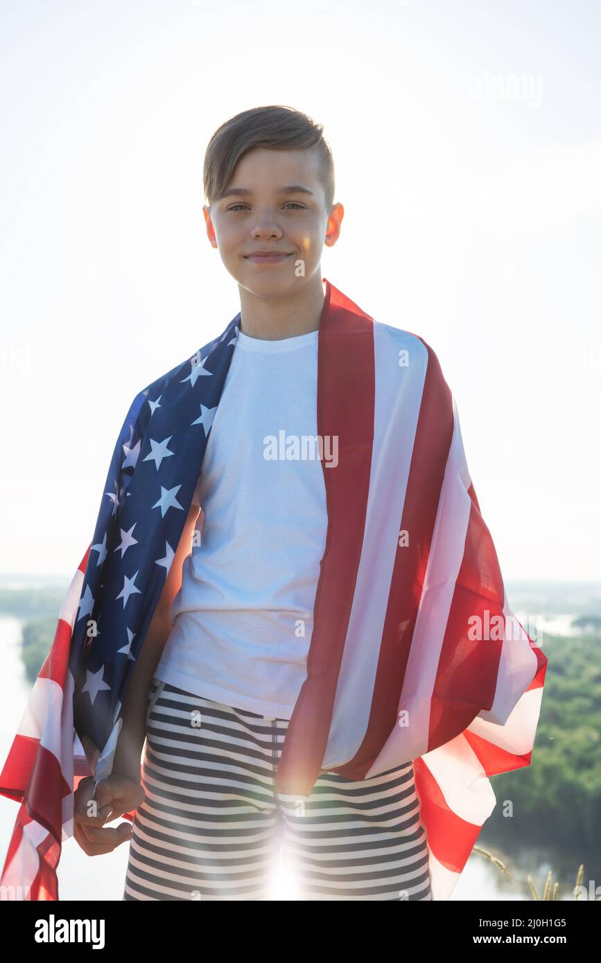Blonde boy waving national USA flag outdoors over blue sky at the river ...