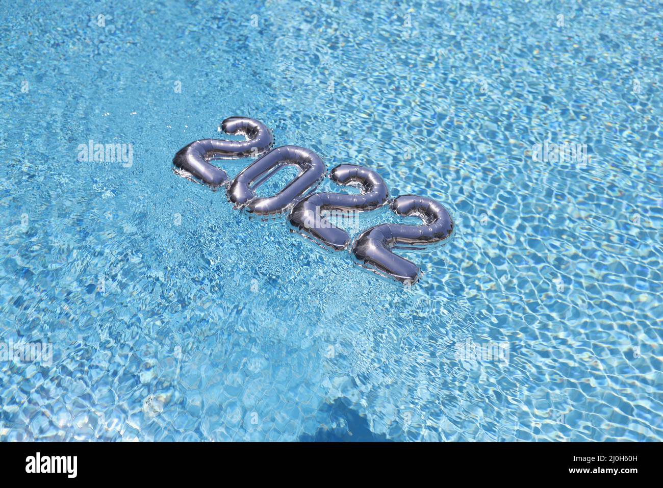 Silver foil numbers floating on blue clean swimming pool water, festive ...