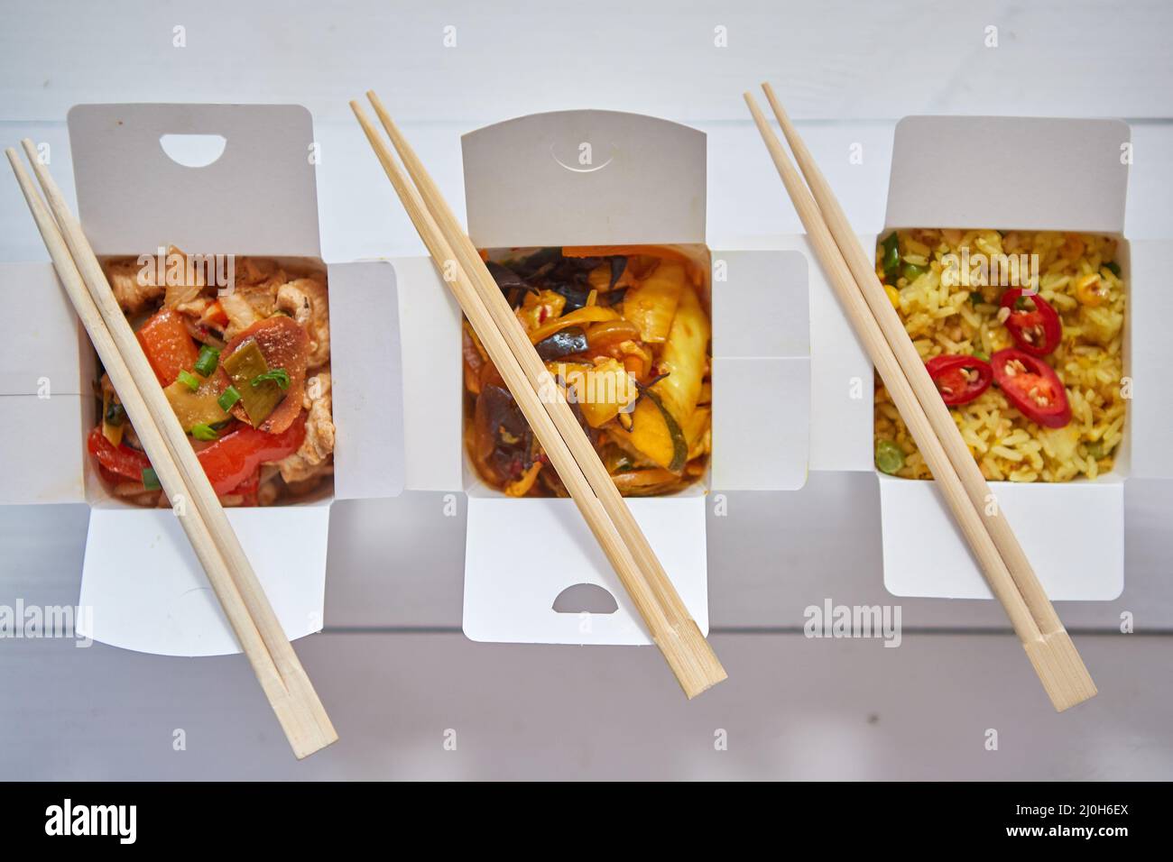Three take away paper boxes filled with asian food placed in row on ...