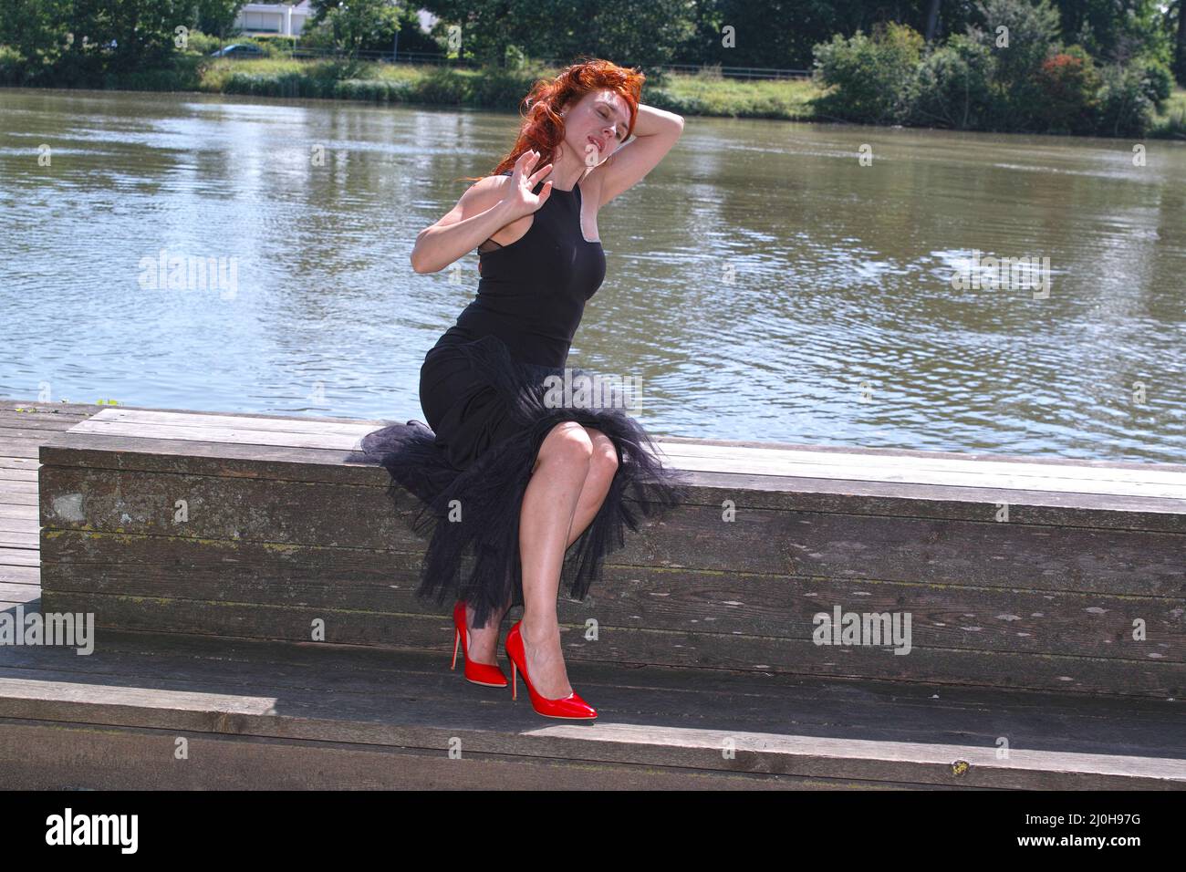 young woman in black dress running fingers through red hair Stock Photo ...