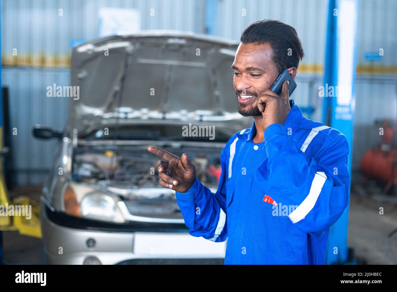 Smiling car mechanic talking on mobile phone with customer in front of ...