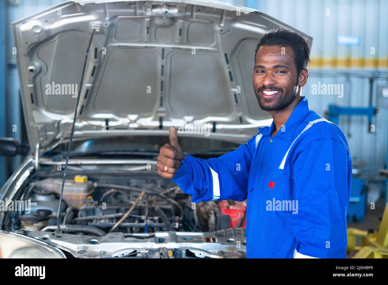 young car mechanic working by showing thumb up by looking at camera at ...