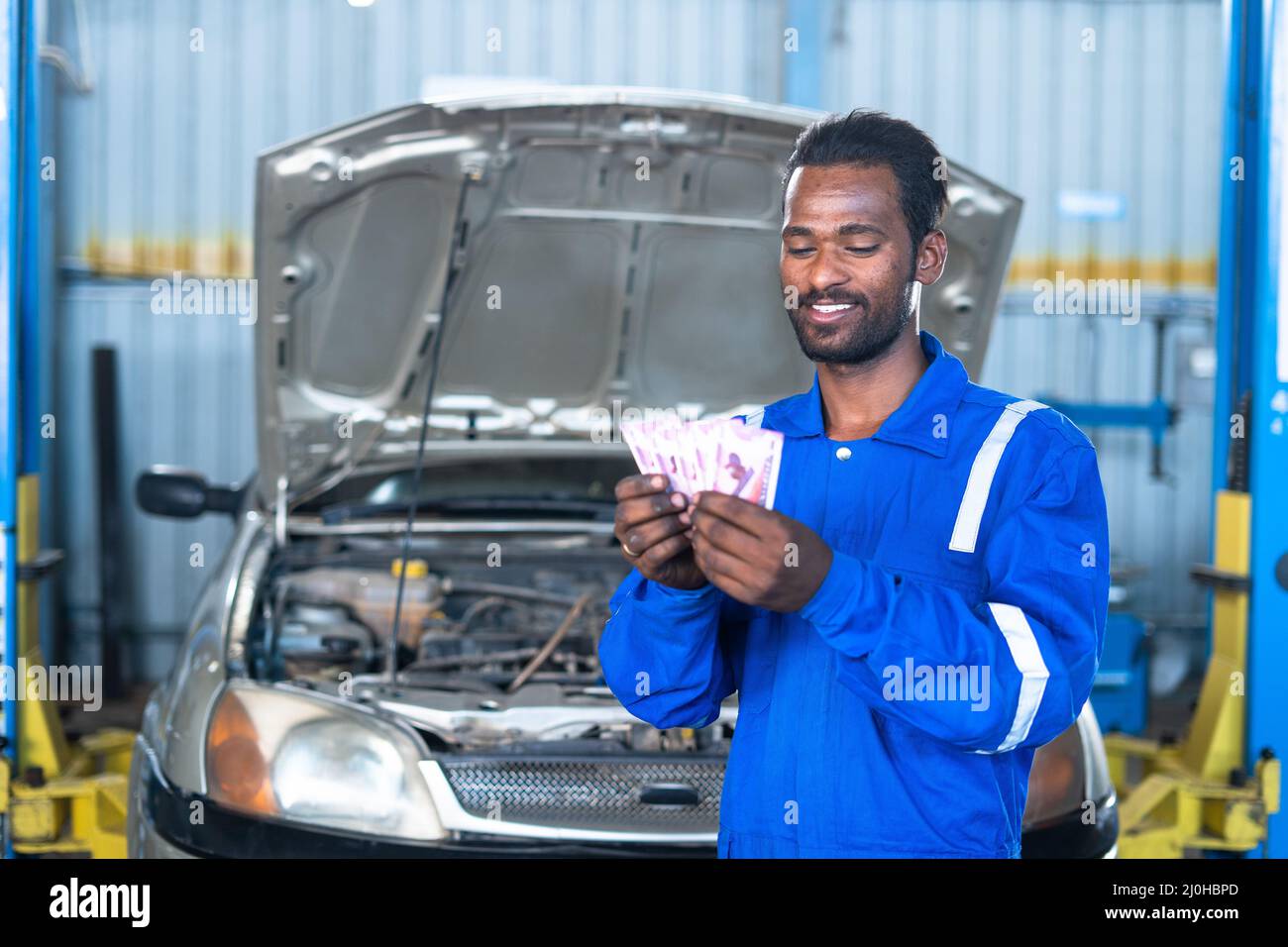 Mechanic in front of car at garage couting Indian currency notes ...