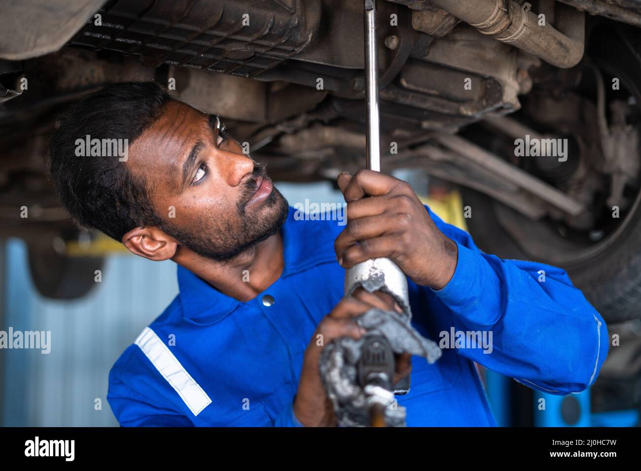 Car mechanic in uniform busy working using tools in under lifted ...