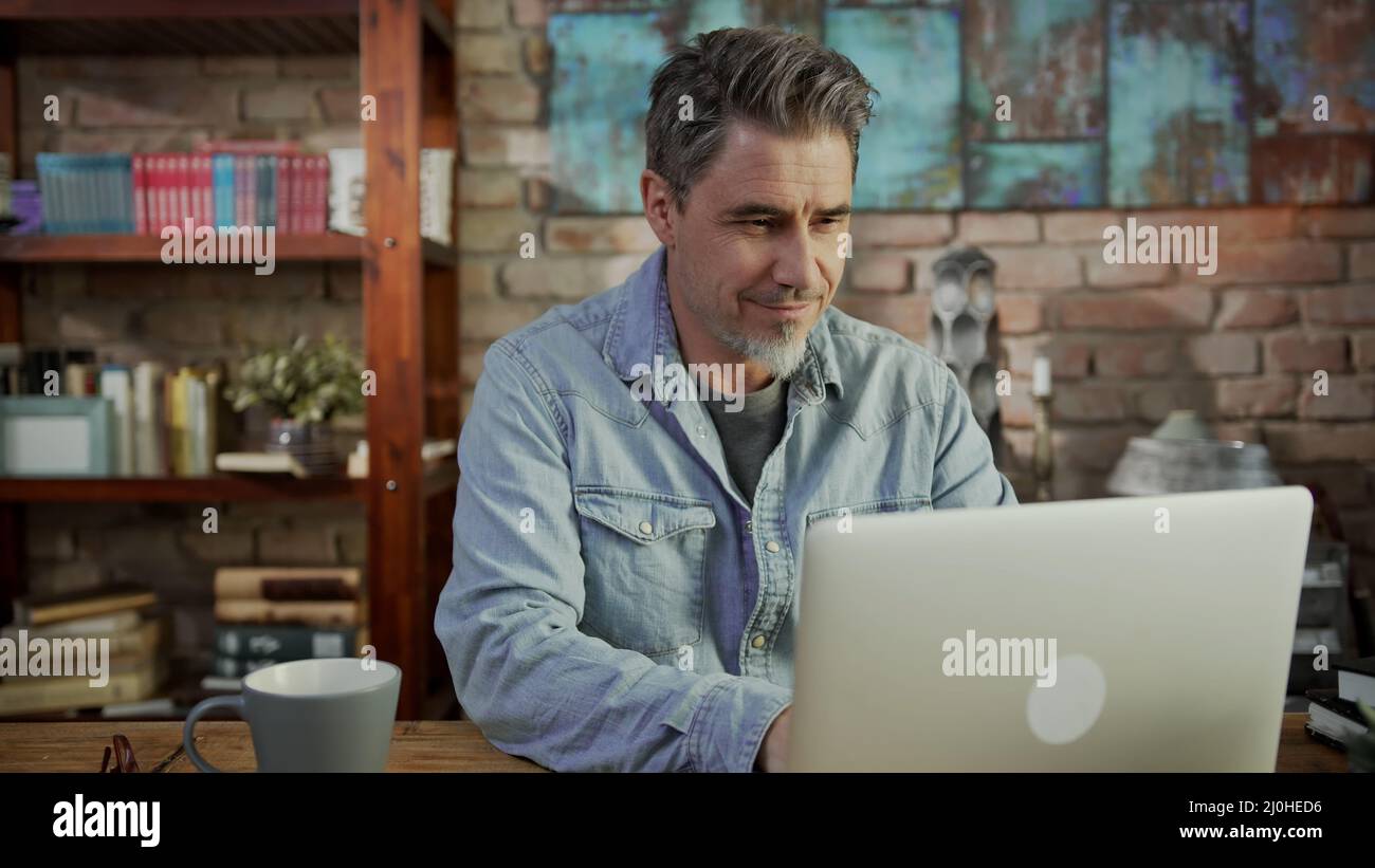 Mature man working alone from home. Sitting at desk teleworking online ...