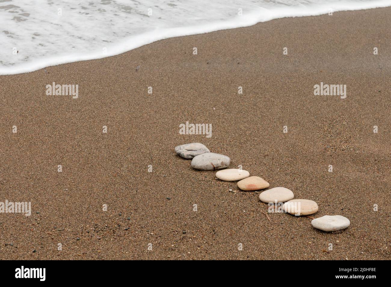 Smooth beach stones in a raw on a sandy coastline and foam of sea water ...