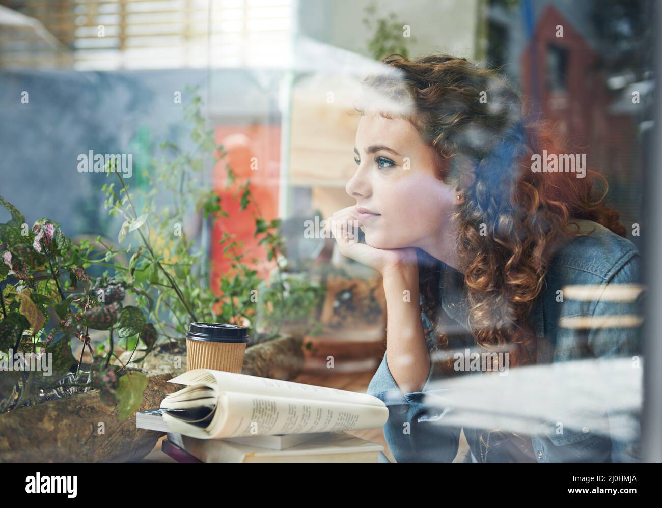 Daydreaming in her favorite spot by the window. A young woman looking ...