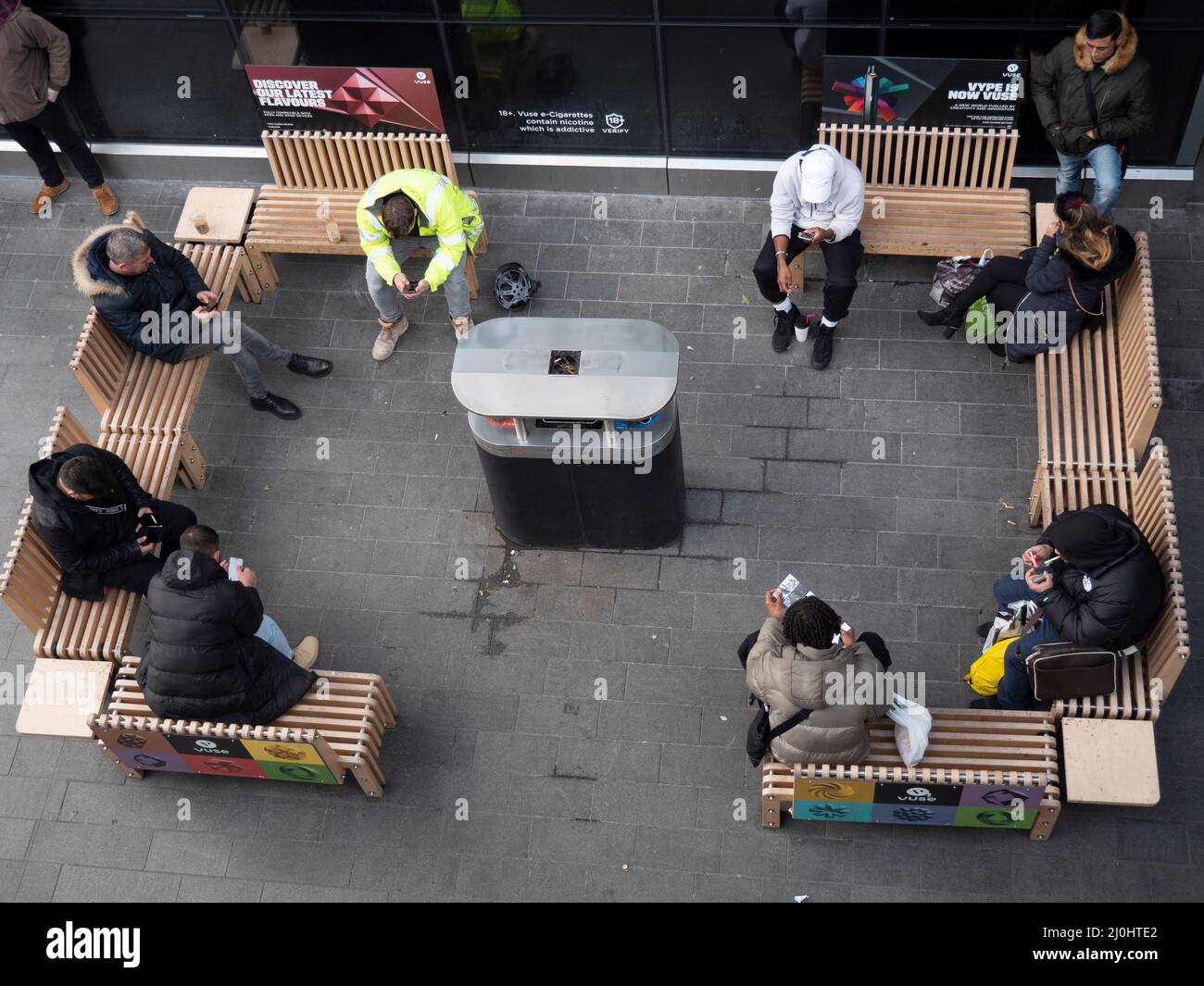Smokers congregate in outdoor smoking area, and look at the screens of ...