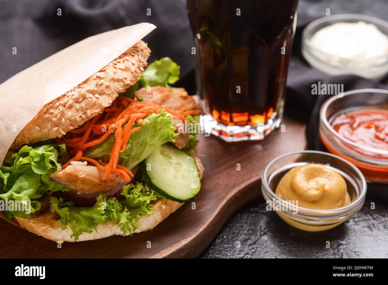 Fresh doner kebab in bun with sauces and glass of cola drink on dark ...