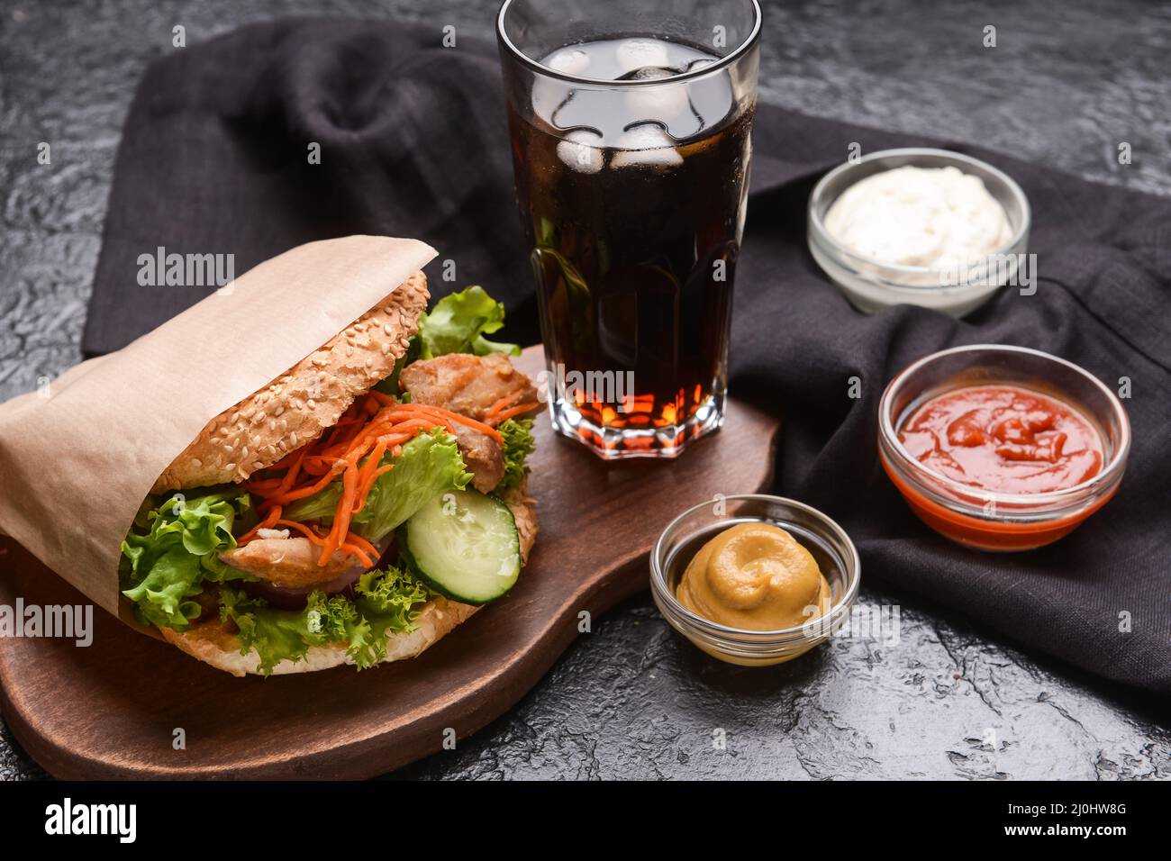 Fresh doner kebab in bun with sauces and glass of cola drink on dark ...