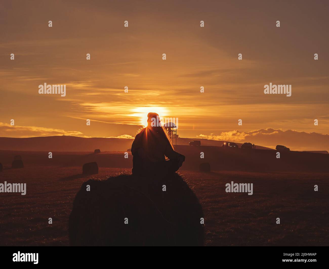 Silhouette of a girl sitting on haystack in a field high in the ...