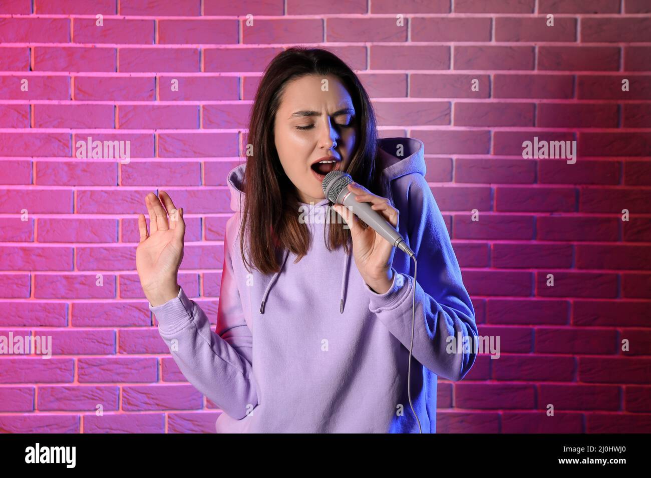 Cool young woman singing on color brick background Stock Photo - Alamy