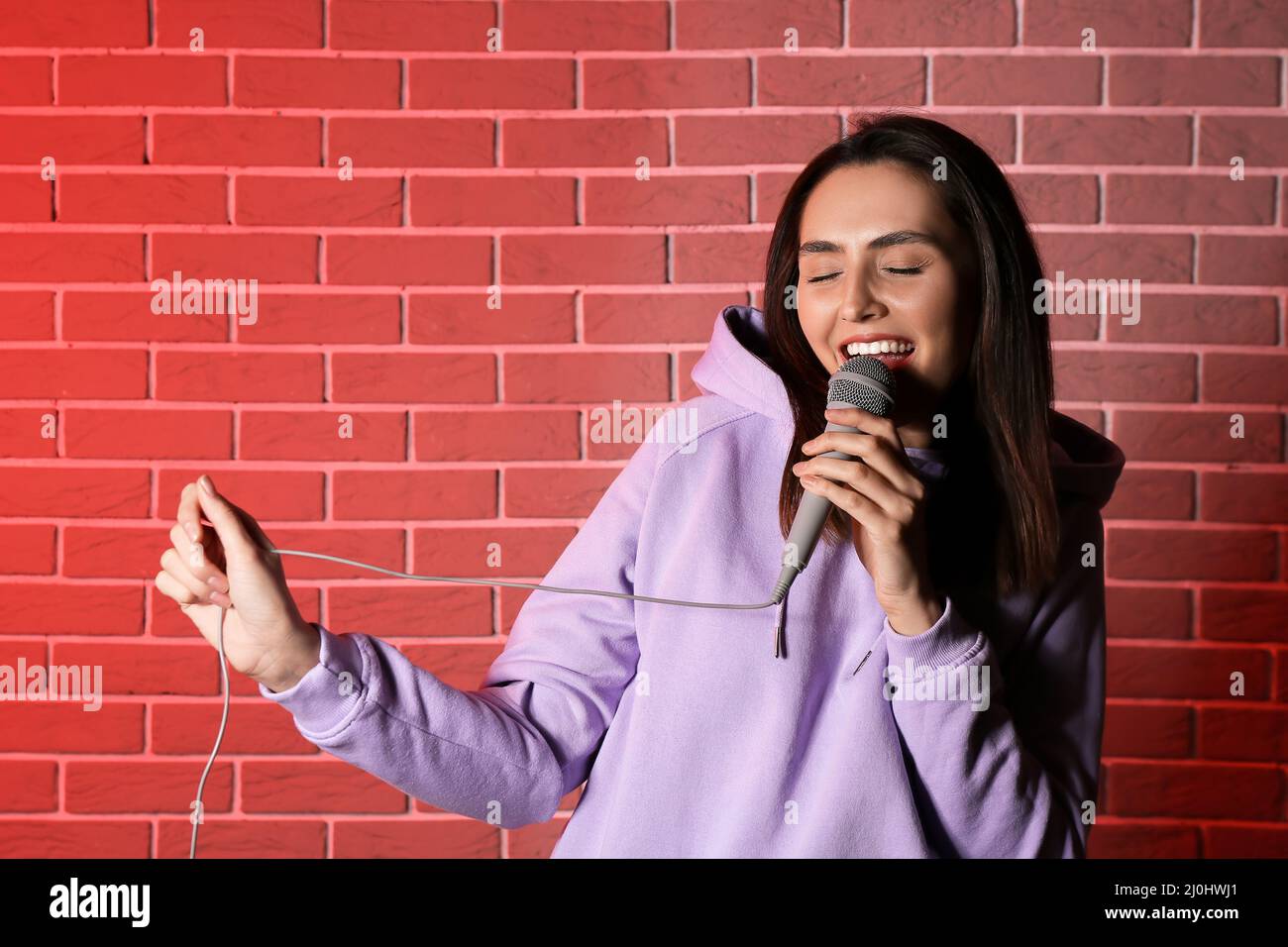 Cool young woman singing on color brick background Stock Photo - Alamy