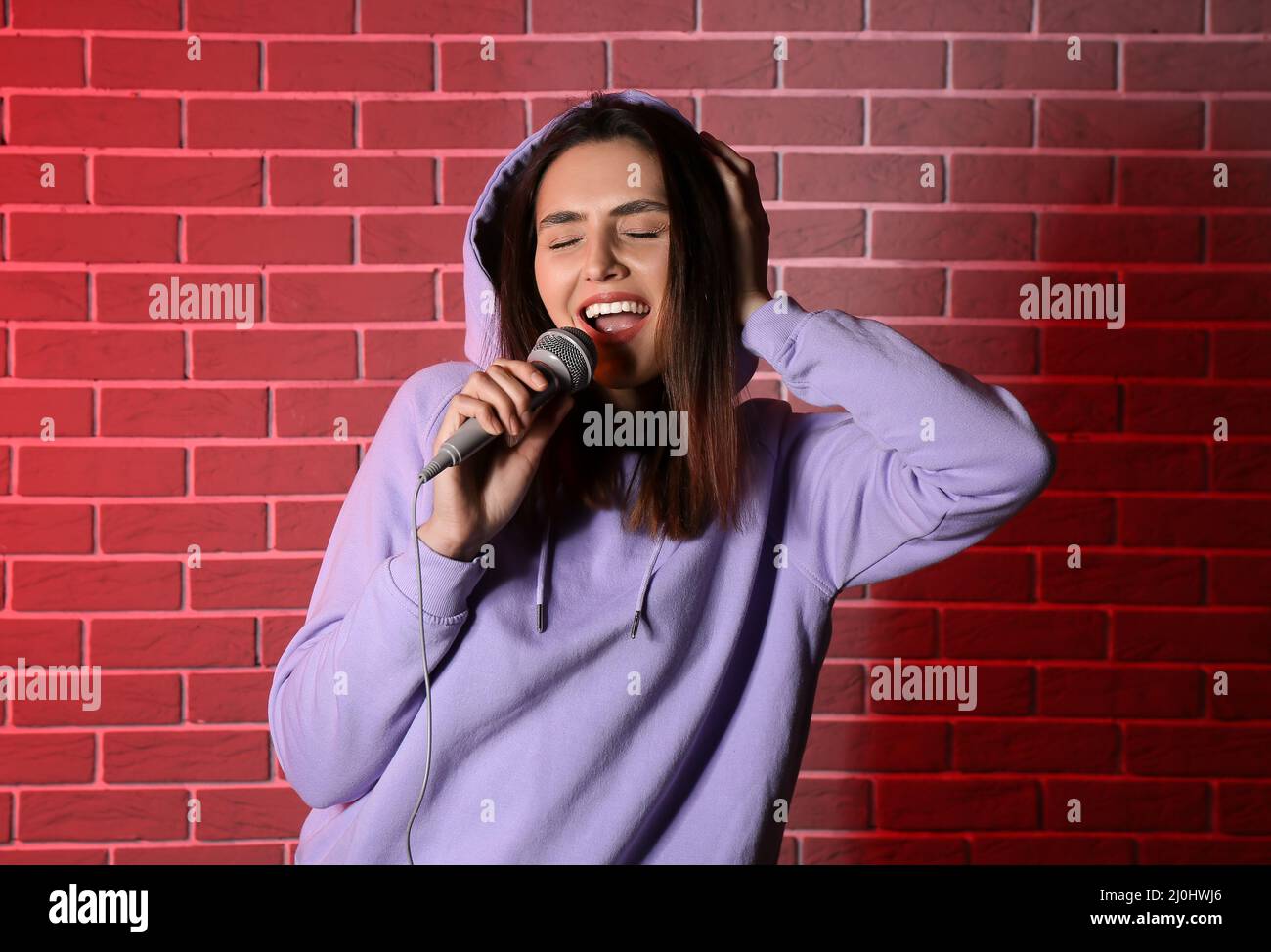 Cool young woman singing on color brick background Stock Photo - Alamy