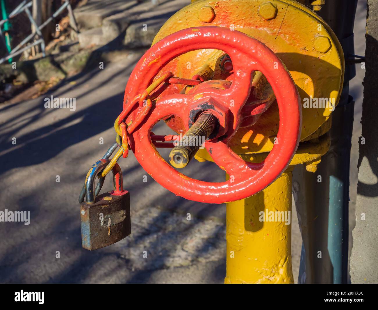 A metal red valve with lock hanging from a chain on a yellow pipe ...