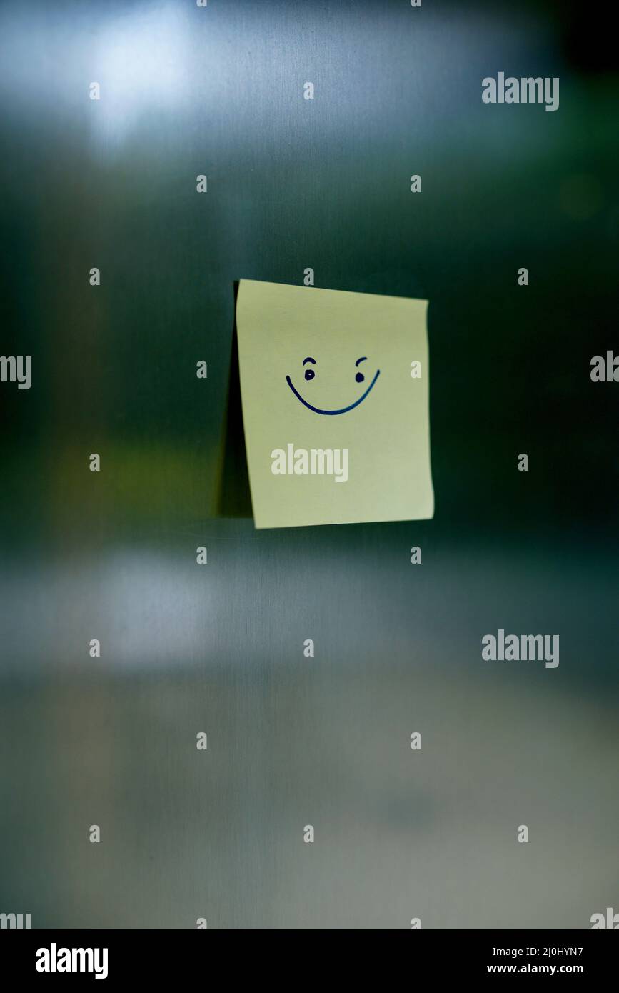 Closeup of a Smiley Face yellow sticky note on a shiny wall background ...