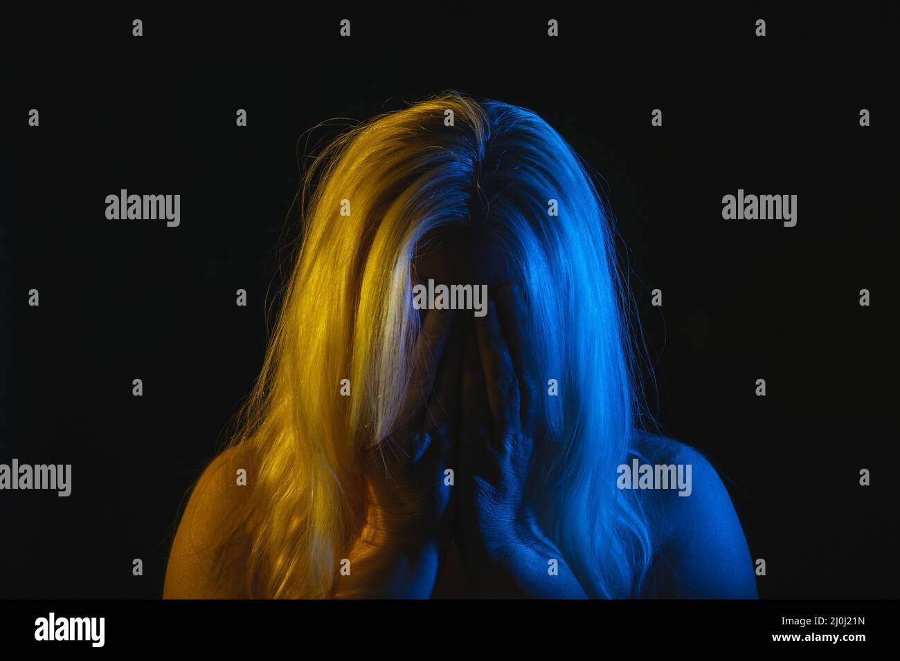 Woman with long hair crying in her hands, illuminated with Ukraine flag ...