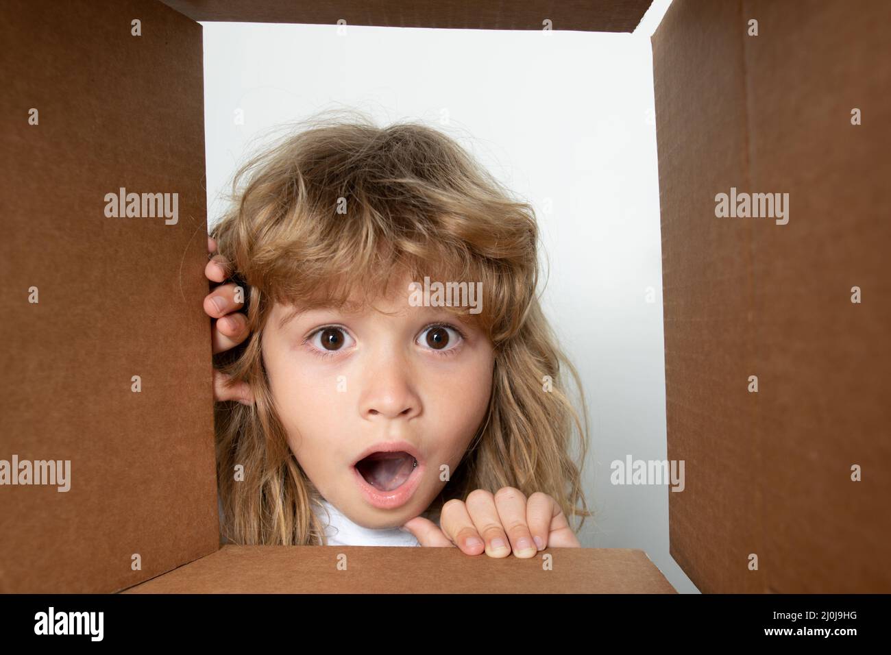 Happy little child boy is opening gift and looking inside cardboard box ...